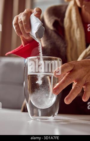 Woman pouring powder from medicine sachet into glass with water at ...