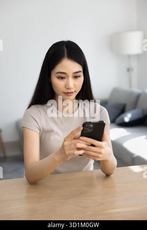 Asian woman using smartphone at home sitting on comfortable sofa ...