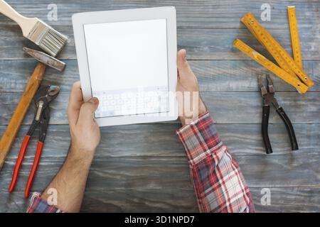Hands holding construction tools and tablet computer on red background ...