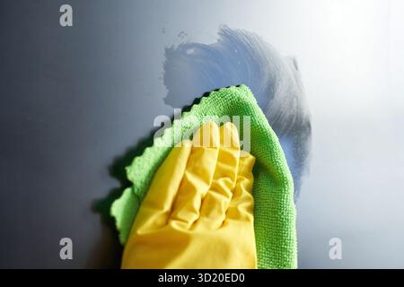 Close up of yellow gloved hand cleaning surface with green cloth and ...