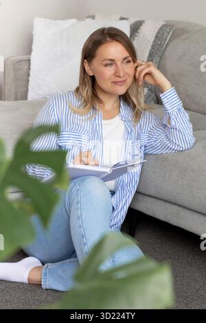 Reflective woman writing in journal at home for personal development ...
