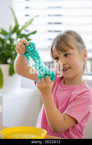 A cute girl playing with bright, blue slime, enjoying a fun and ...