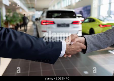 buyer and seller at car dealership shaking hands after buying a car ...
