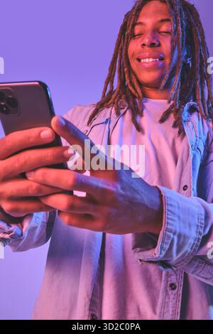 Young man with dreadlocks browsing mobile phone at night in downtown ...