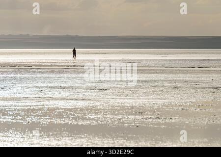 Person walks in shallow water at sunset, with waves and a tranquil ...