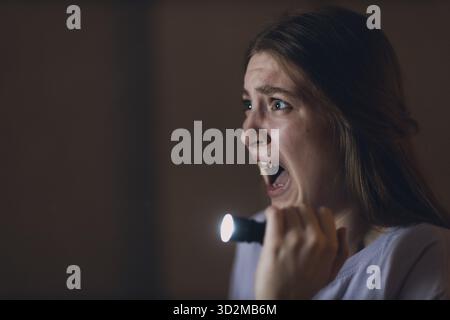 Woman scared holding hand flashlight in darkness and afraid of violence ...