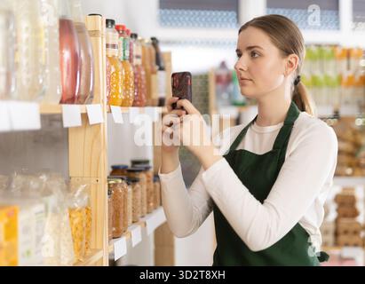 Merchandiser girl takes pictures of goods on supermarket shelves ...
