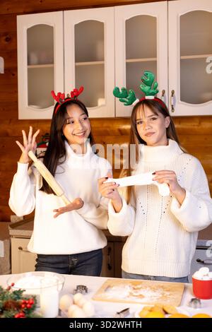 Cute girls in aprons and hats reading recipe book together while ...