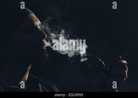 Man smokes smoking pipe against dark background. Back side lit profile ...