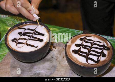Two coffee cups with intricate latte art sit on a marble table, next to ...