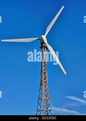 A vertical shot of tall wind turbine in the field on blue sky ...