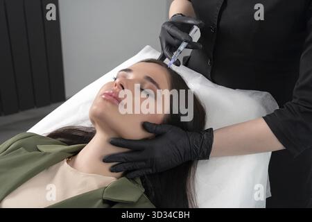 Young woman with hair problem receiving injection in head skin in a ...