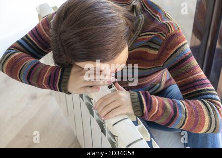 Woman wearing pullover sitting near heater radiator and hugs it Stock ...