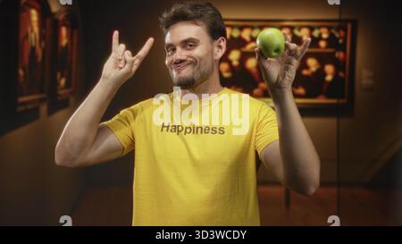 Man makes rock horns with one hand and holds green apple near painting ...