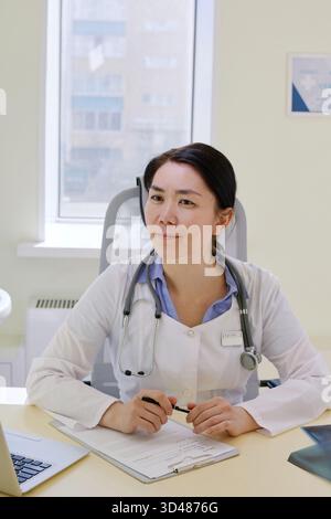 Asian medical professional sitting at desk using laptop while talking ...