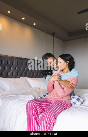 Hugging diverse female partners sitting on bed in modern bedroom, with ...