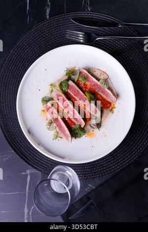 Seared tuna steak with pink center on white plate. Cherry tomatoes ...