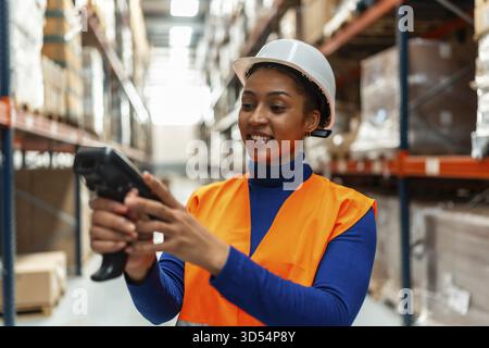 Scanning woman in hard hat and vest, operating handheld barcode scanner ...
