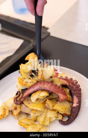 A closeup of octopus tentacle with potatoes on a black background, on a ...
