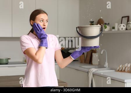 Shocked young woman placing bucket under water dripping from ceiling at ...