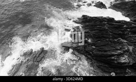 Aerial monotone view of rugged coastal rocks with waves breaking below ...
