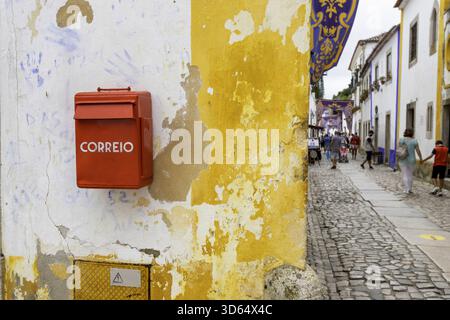 A weathered yellow mailbox stands on a metal post behind a barbed wire ...
