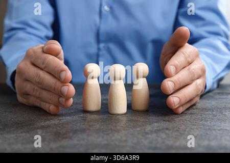 Man protecting human figures at grey table, closeup Stock Photo - Alamy