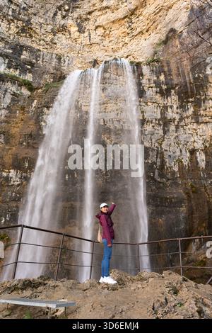 Happy young woman enjoys scenic mountain view sitting on net above ...