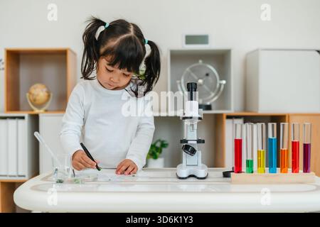 toddler girl scientist using tongs putting small herbal sample in slide ...