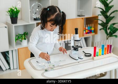 toddler girl scientist using tongs putting small herbal sample in slide ...
