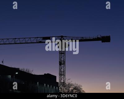 A construction crane stands tall at sunset, its long arms reaching for ...