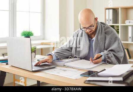 Frozen young man working with laptop in office during blackout Stock ...