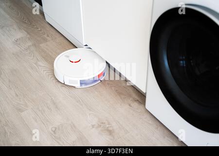 Robot vacuum cleaner moving near washing machine on wooden floor inside ...