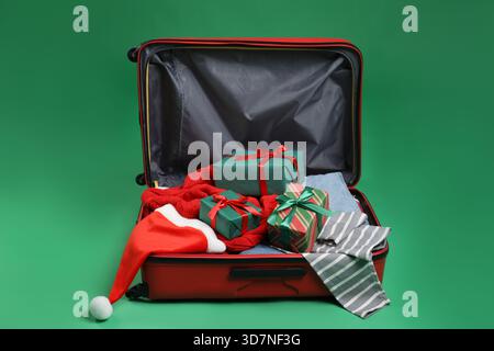 Christmas vacation. Open suitcase with Santa hat, clothes, gift boxes ...