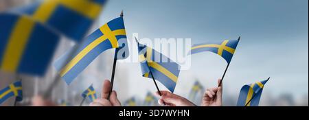 Sweden flags in their hands on a blurred urban background. The photo ...