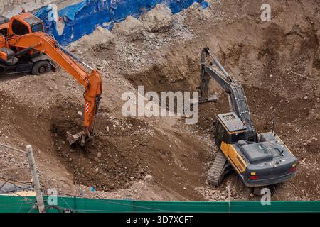 Two excavators dig through layers of soil and rock, coordinating their ...