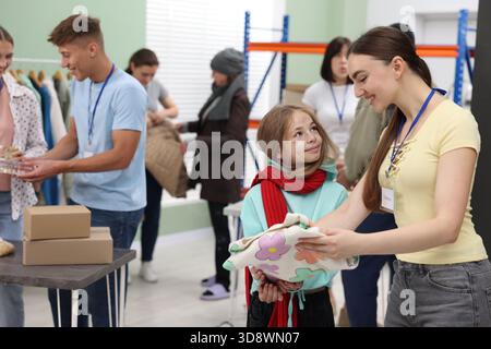 Happy volunteer giving clean clothes to homeless girl in shelter Stock ...