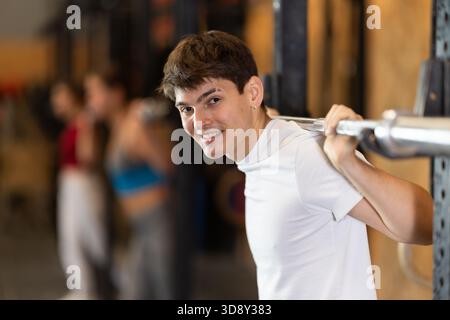 Slender guy trains muscles of arms and back using barbell and ...