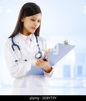 Asian female doctor writing medical records sitting at desk in modern ...