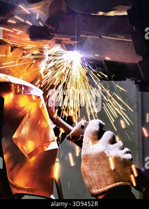 Mechanic in protective gloves cutting metal with red handheld grinder ...