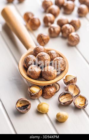 Wooden bowl and spoon with tasty macadamia nuts on blue background ...