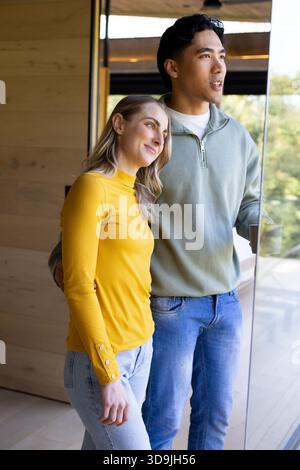 Diverse couple gazing through glass sliding door in cabin with wooden ...