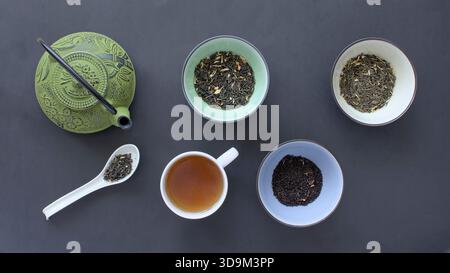 Composition with cup of black tea, teapot and dry leaves on grey tile ...
