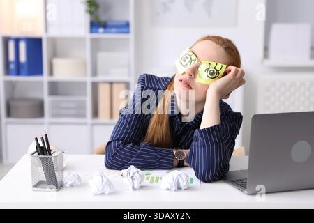 Woman with fake eyes drawn on sticky notes snoozing at workplace in ...