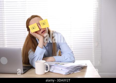 Woman with fake eyes drawn on sticky notes snoozing at workplace in ...