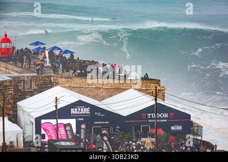 A surfer rides a towering wave off Praia do Norte as spectators crowd ...