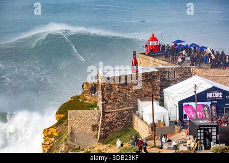 A surfer rides a towering wave off Praia do Norte as spectators crowd ...