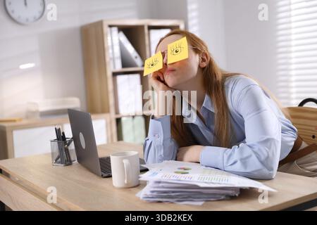 Woman with fake eyes drawn on sticky notes snoozing at workplace in ...