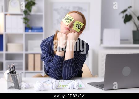 Woman with fake eyes drawn on sticky notes snoozing at workplace in ...