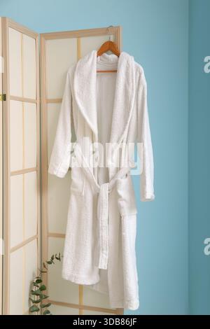 White bathrobe hanging on folding screen against yellow background ...